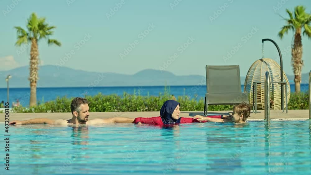 A young woman wearing a hijab swimsuit is swimming in the pool with her ...
