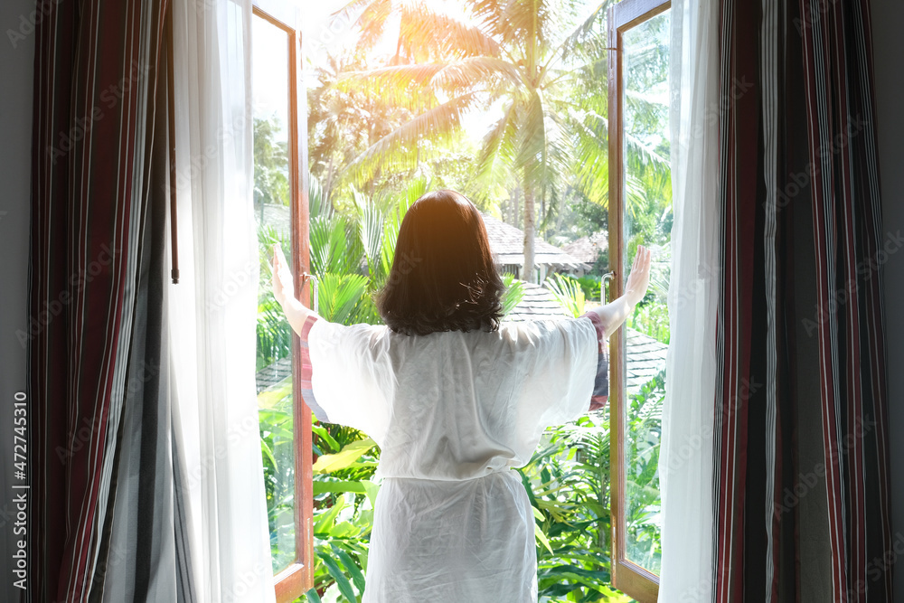 A woman opens a window to welcome the morning sunlight of a new day at ...