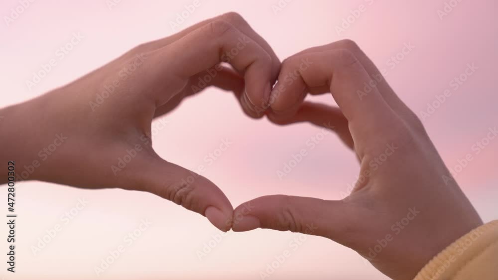 girl shows heart shape at pink sunset in the sky, romantic valentine ...