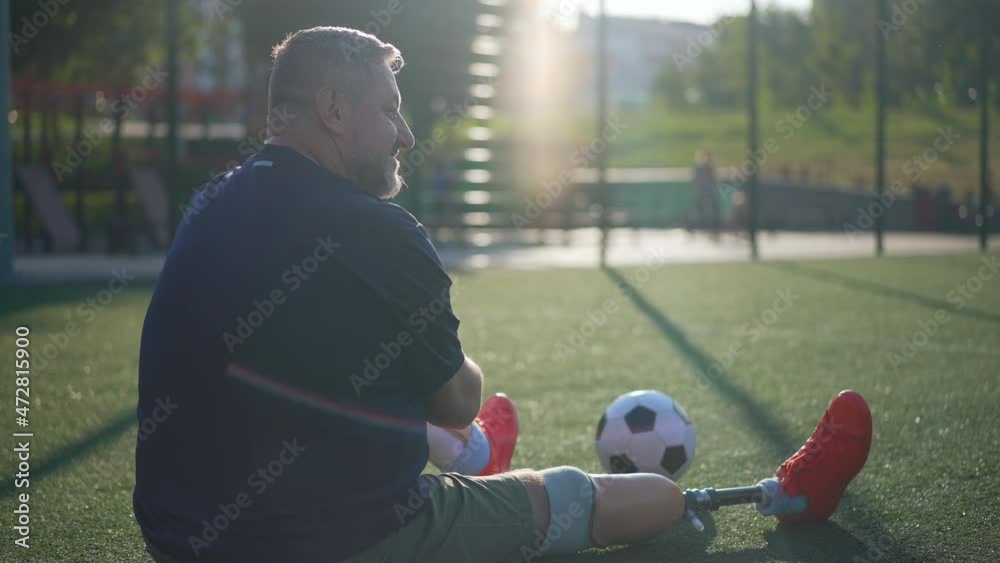 Relaxed confident male mature amputee in sunlight sitting on stadium ...