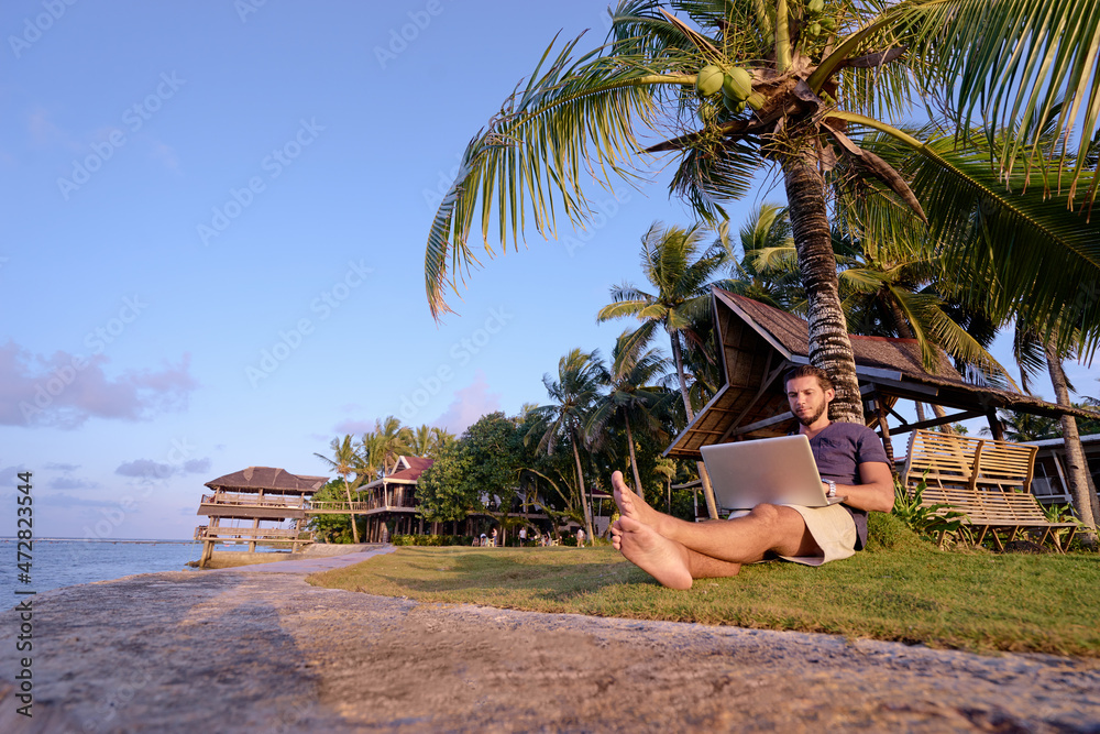Work and vacation. Young man working on laptop computer on the tropical ...