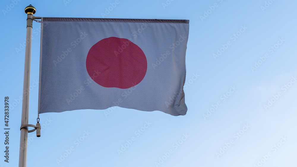 National flag of Japanese on a flagpole in front of blue sky with sun ...