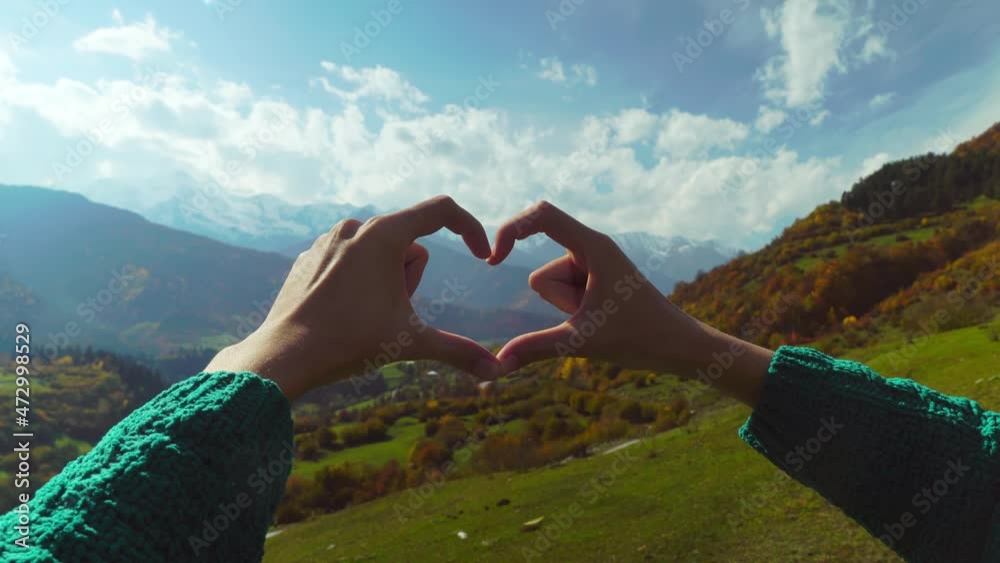 Woman on hike on top of mountain makes heart shaped finger frame with ...