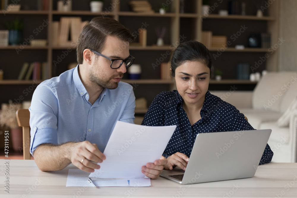 Two diverse coworker employees sharing laptop, discussing paper report ...