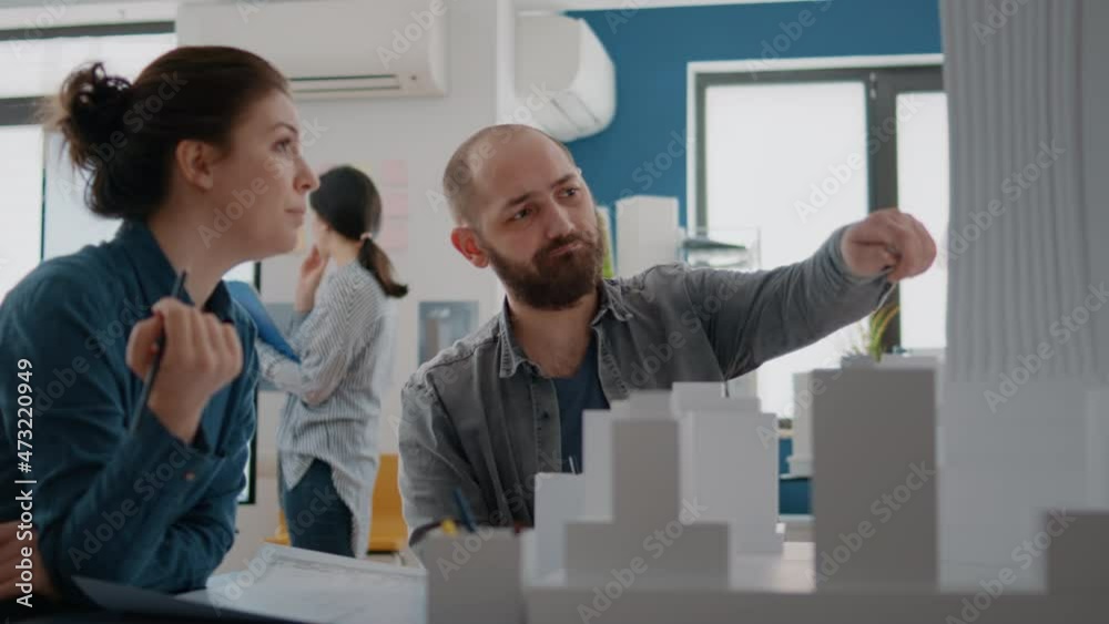 Man and woman pointing at building model to plan blueprints on paper ...