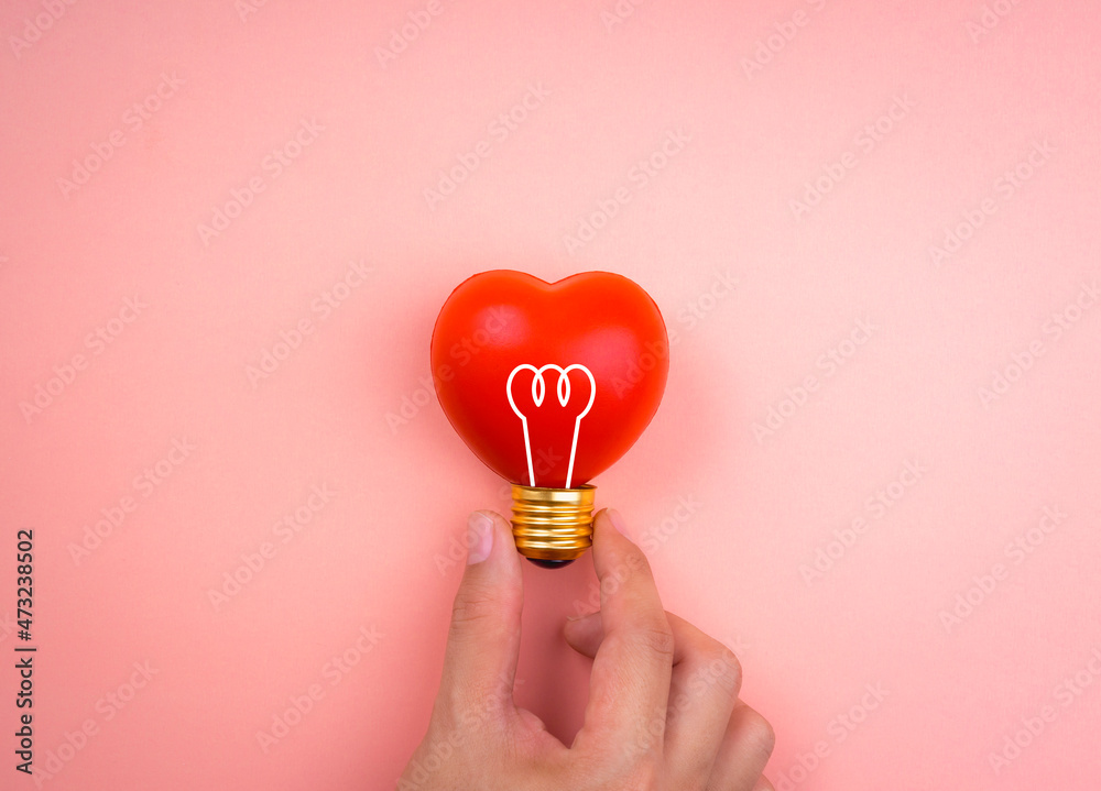 Hand holding light bulb icon symbol on red heart ball on pink pastel ...