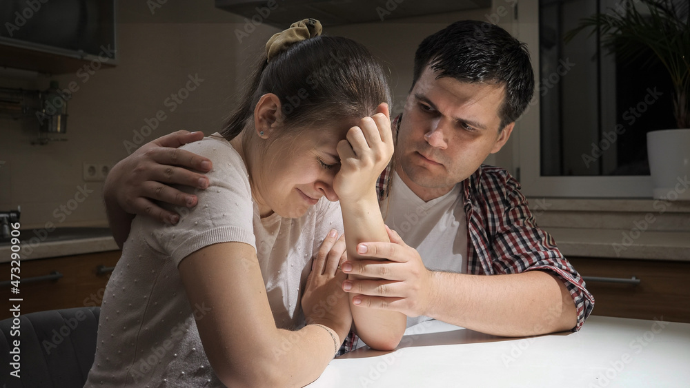 Young man consoling and hugging his crying wife on kitchen at night ...