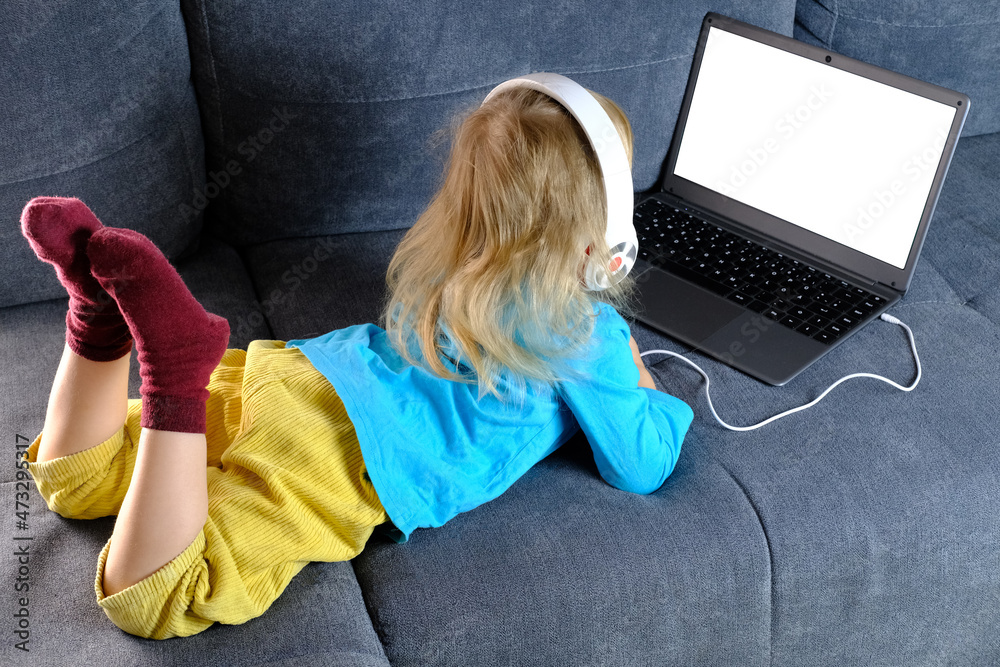 child 2-3 years old, girl in headphones lies on sofa in front of laptop ...