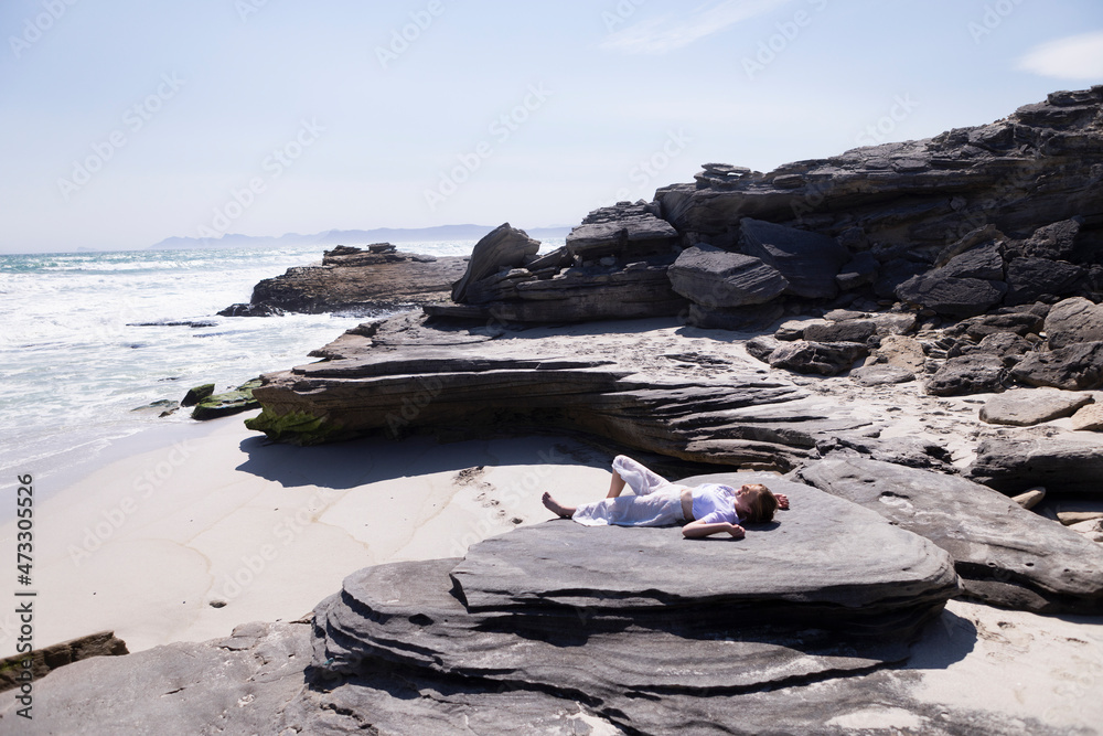 Teenage girl lying on her back on rocks above a sandy beach. Stock ...