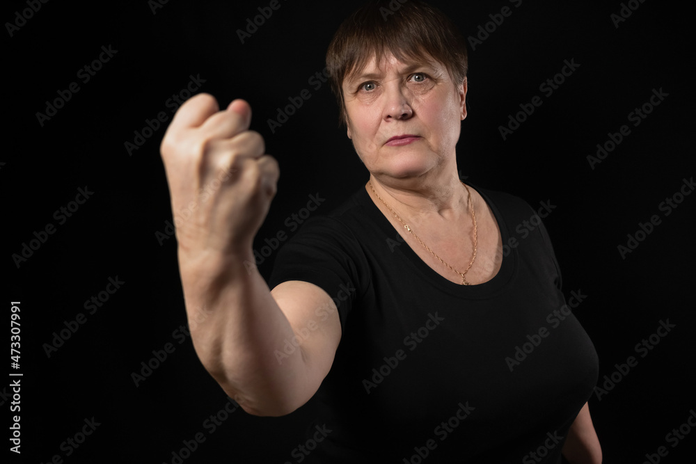 Angry woman shows her fist at you. Elderly woman on a black background ...