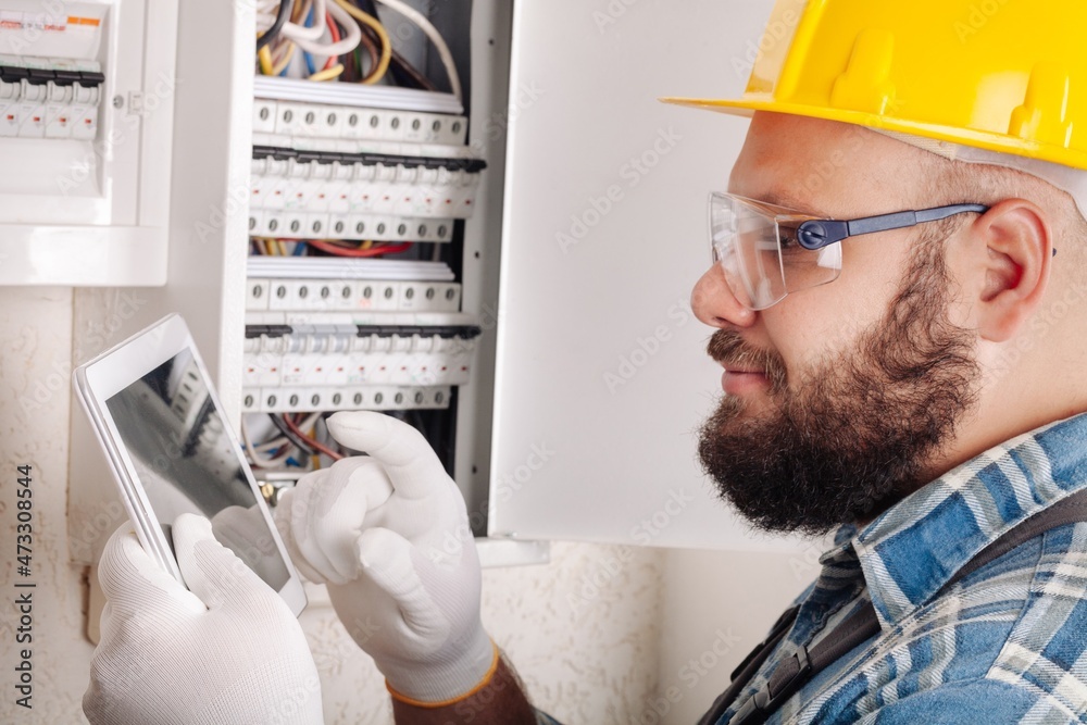 Electrician at work on an electrical panel protected in safety goggles ...