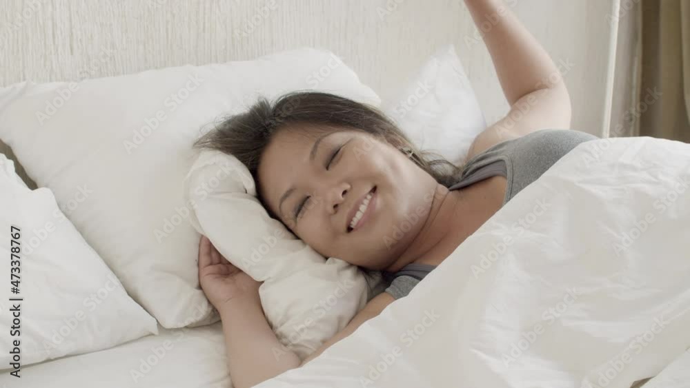 Medium shot of happy Japanese woman waking up and stretching. Beautiful ...