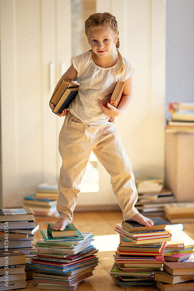 cute little girl is reading book and standing on pile of books ...