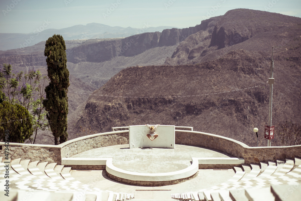 Dancer elevates in geometric amphitheatre with desert sun ridge view ...