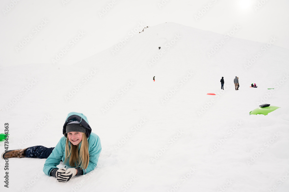 Smiling Young Girl Lying Down at the Bottom of Snowy Sledding Hill ...