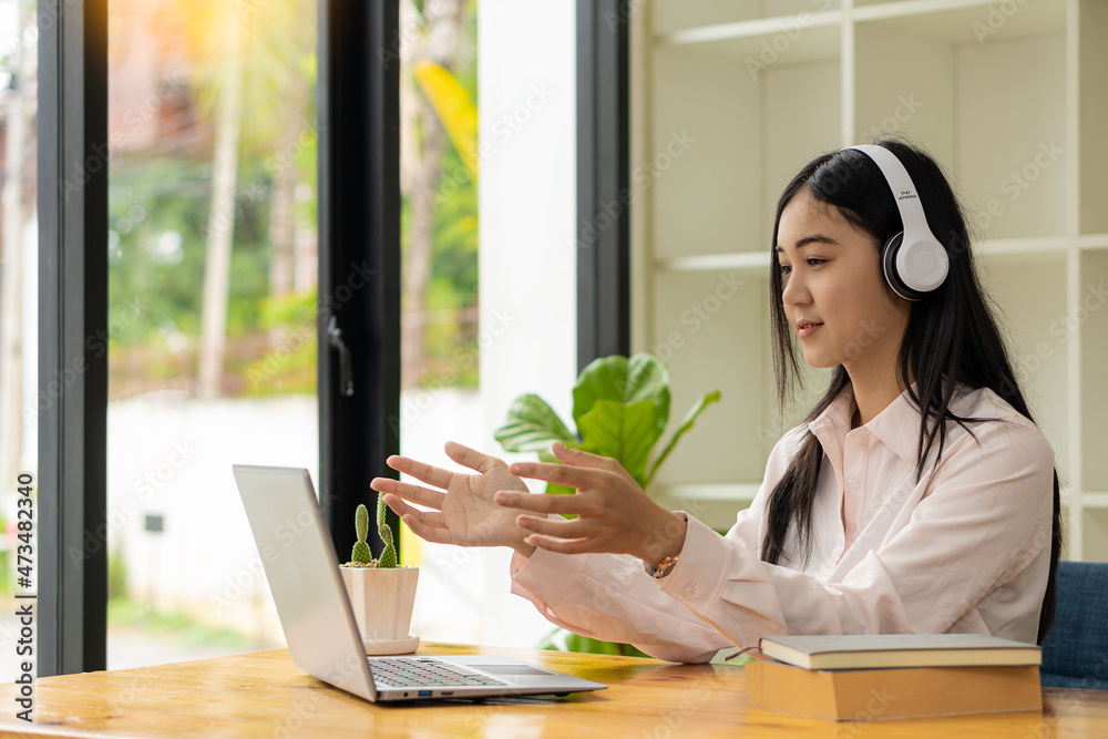 Beautiful Asian student wearing headphones listening to online course development program on ...
