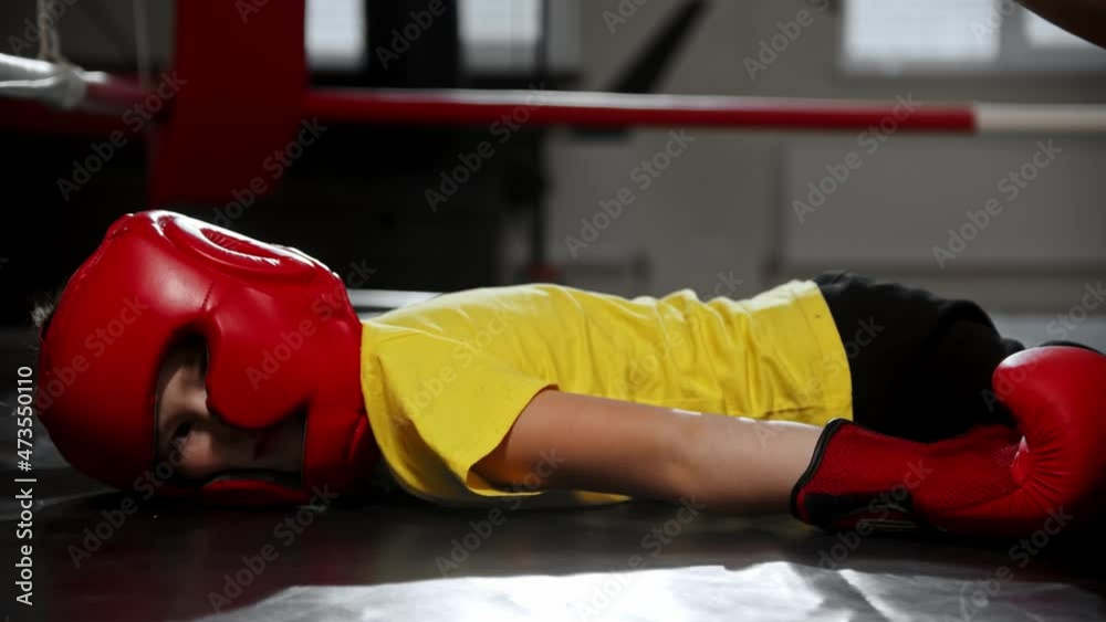 Little boy in boxing gloves and soft helmet falls down on the ring in ...