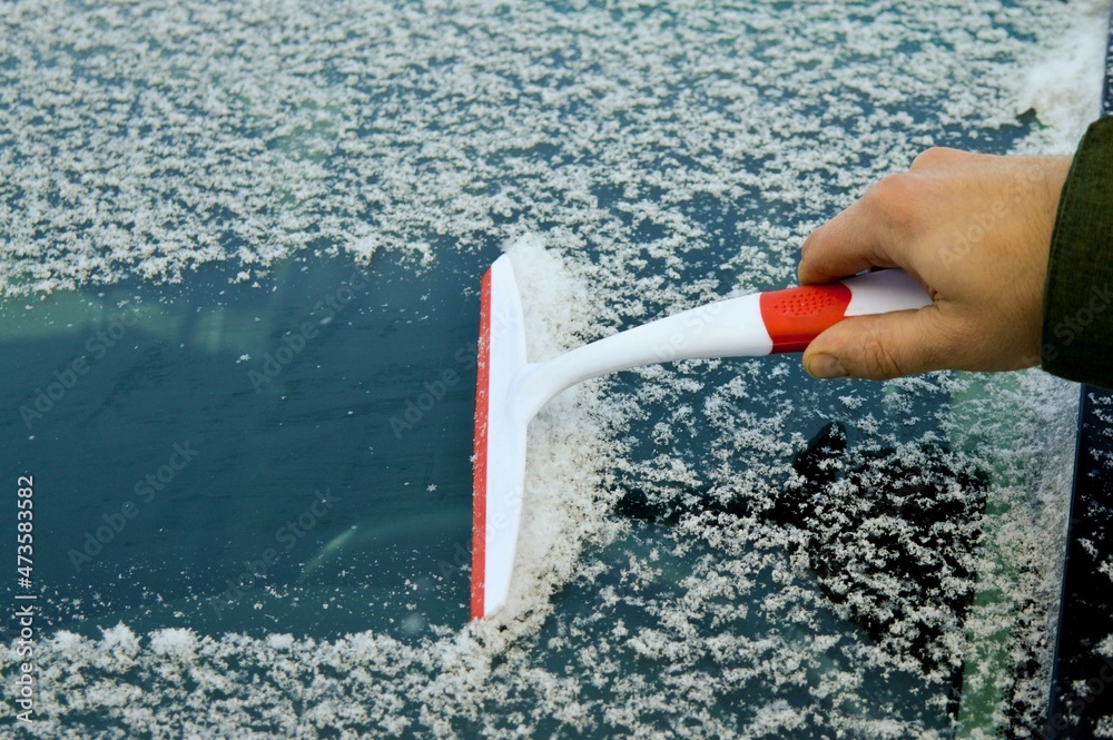 Scraping ice from the car window. Clearing snow from glass and car body ...