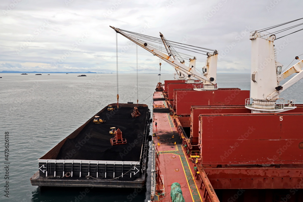 Loading coal from cargo barges onto a bulk carrier using ship cranes ...