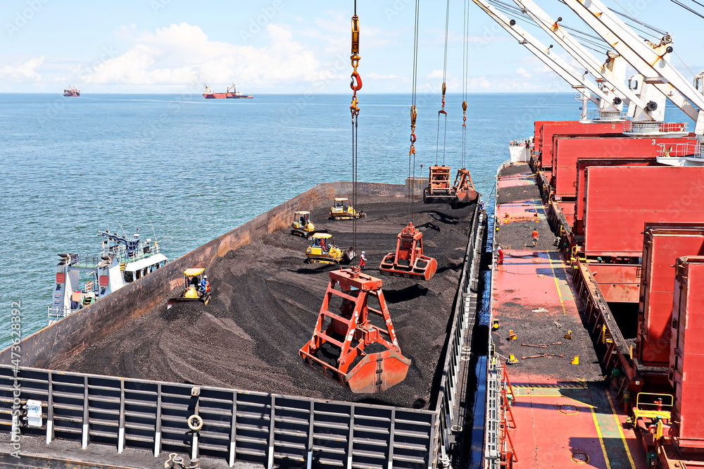 Loading coal from cargo barges onto a bulk carrier using ship cranes ...