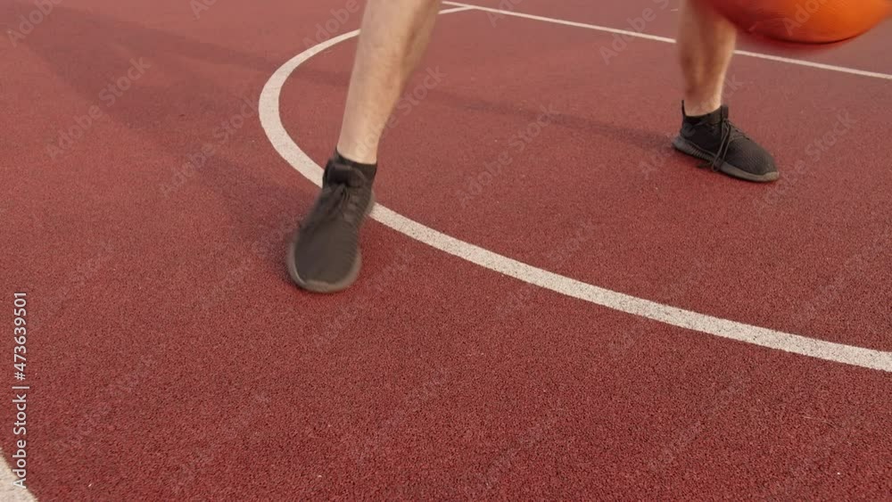 Legs man practicing ball skills by rolling a basketball between his ...