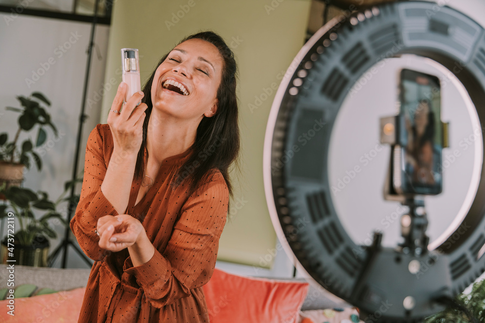 Laughing female influencer holding foundation while vlogging at home foto de Stock | Adobe Stock