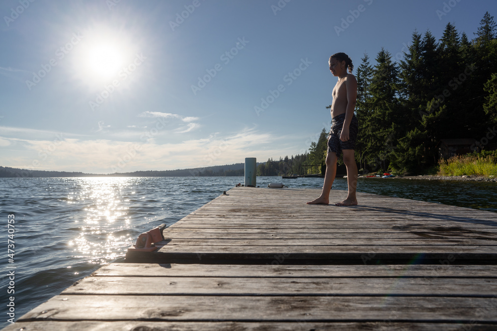 Boy in swimsuit stands on dock by lake Stock Photo | Adobe Stock