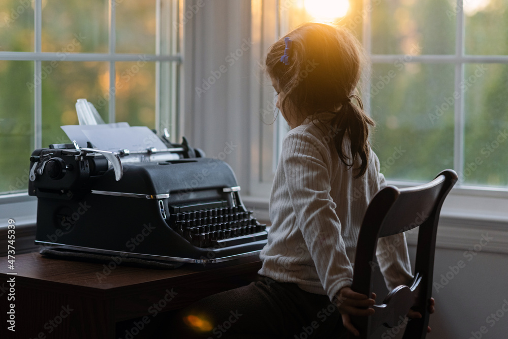 Little girl with typewriter by the window Stock Photo | Adobe Stock