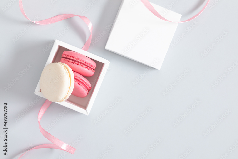 Pink cake macaron or macaroon in white gift box with ribbon on gray ...