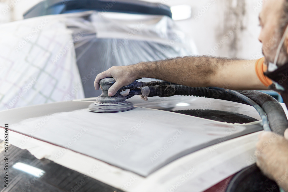 Auto mechanic sanding a part of a car in a garage. Preparing for ...