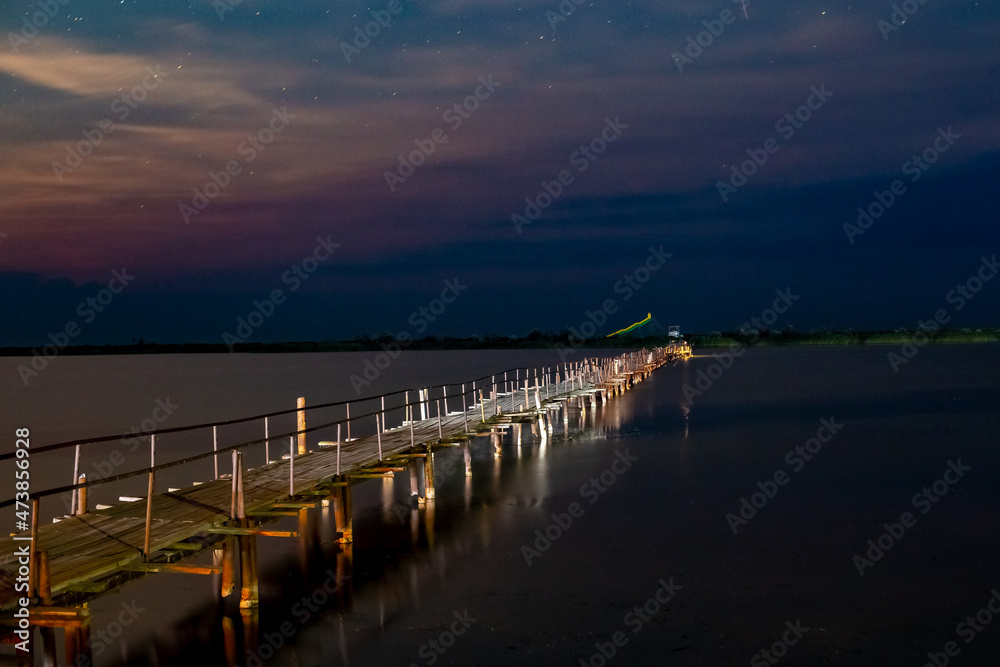 A wooden pedestrian bridge with railings runs along the lake, around ...