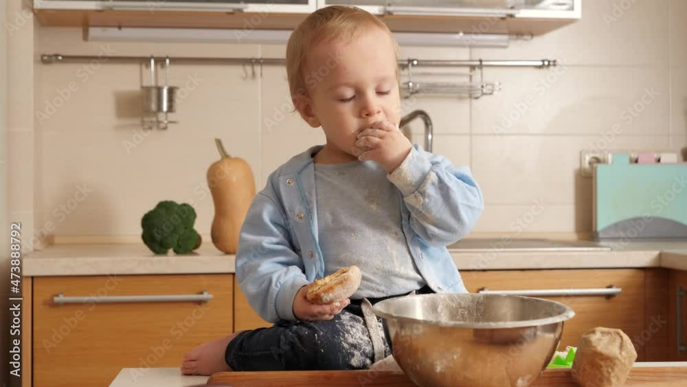 Cute baby boy sitting on kitchen table, playing with flour and eating ...