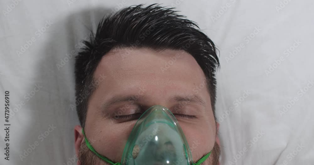 Close-up of a young man opening his eyes in a hospital bed in an ...
