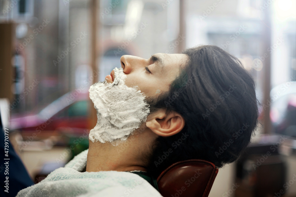 Profile of male customer sitting in barber shop with shaving cream on ...