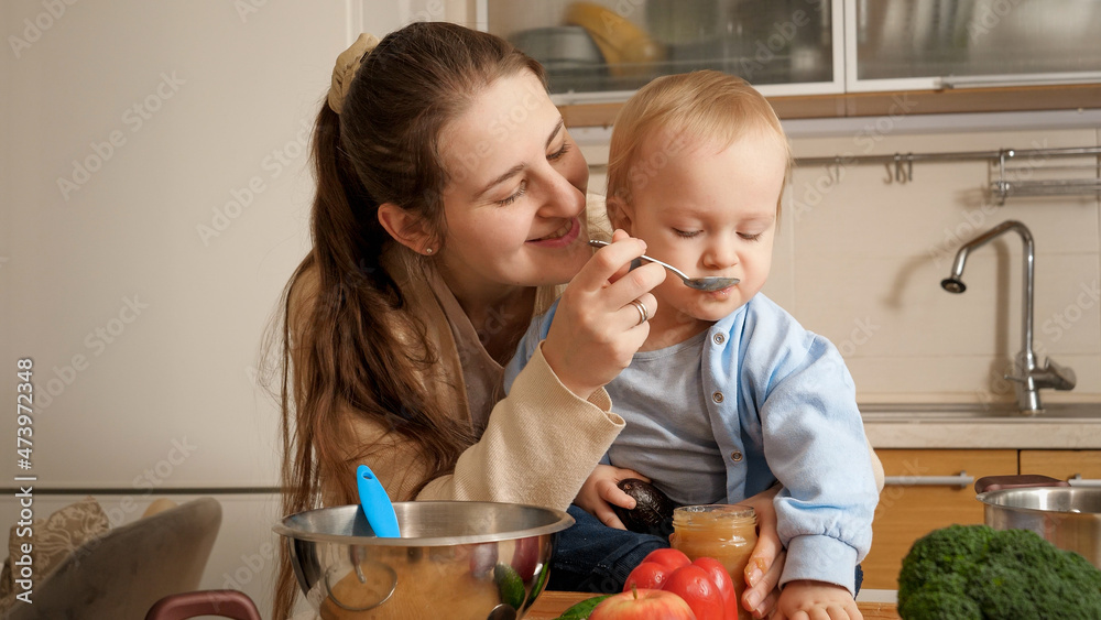 Cute baby boy sitting on kitchen table and playing with cookware while ...