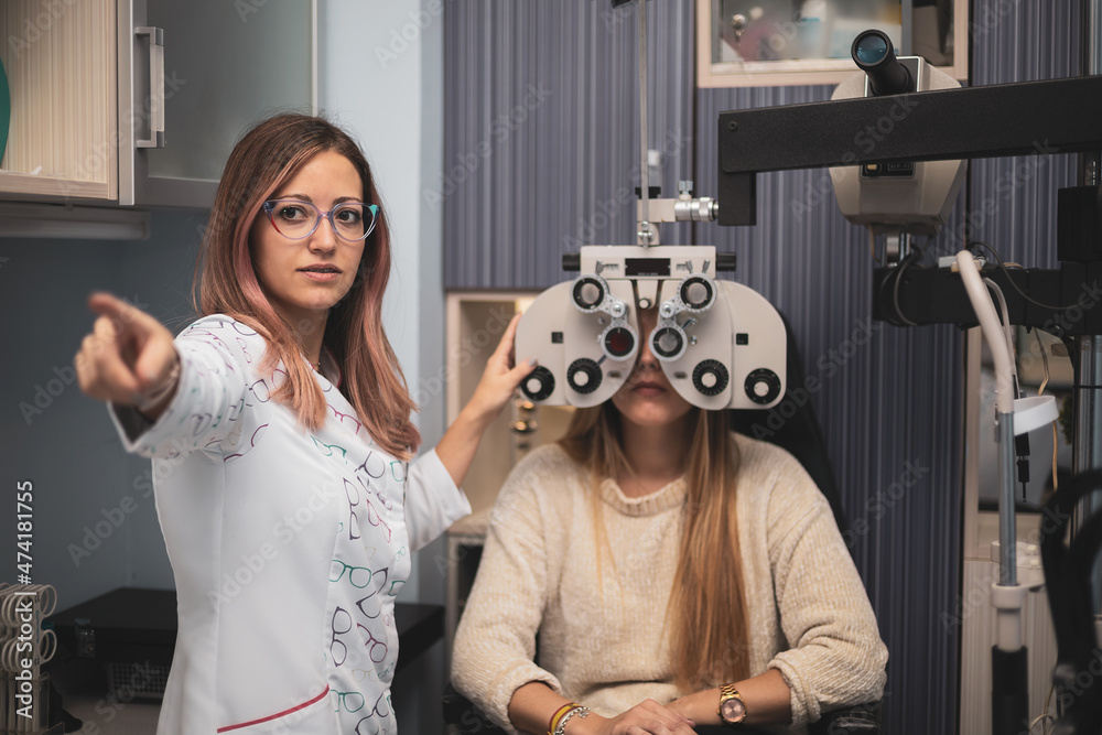 An optometrist directs a patient who uses a phoropter to grade her ...