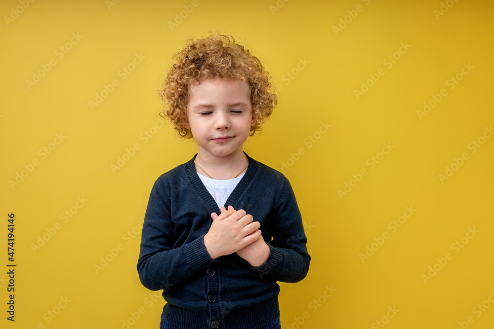 calm Cute caucasian kid boy hold hands on chest near heart, casually ...