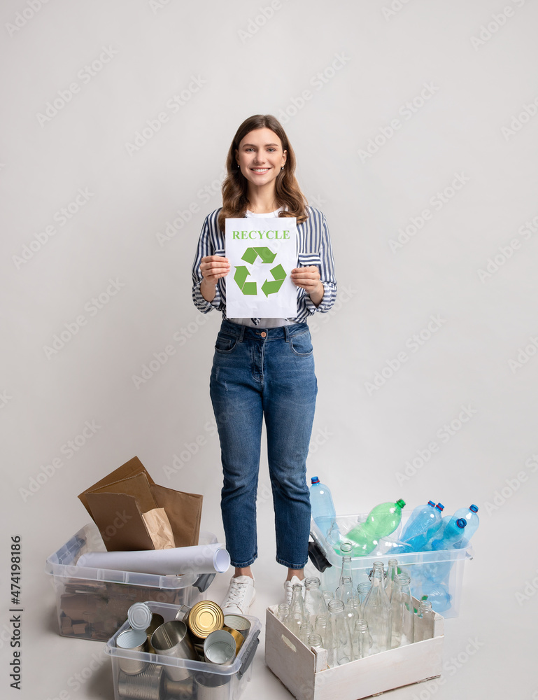 Smiling young female holding placard with recycle sign standing among ...