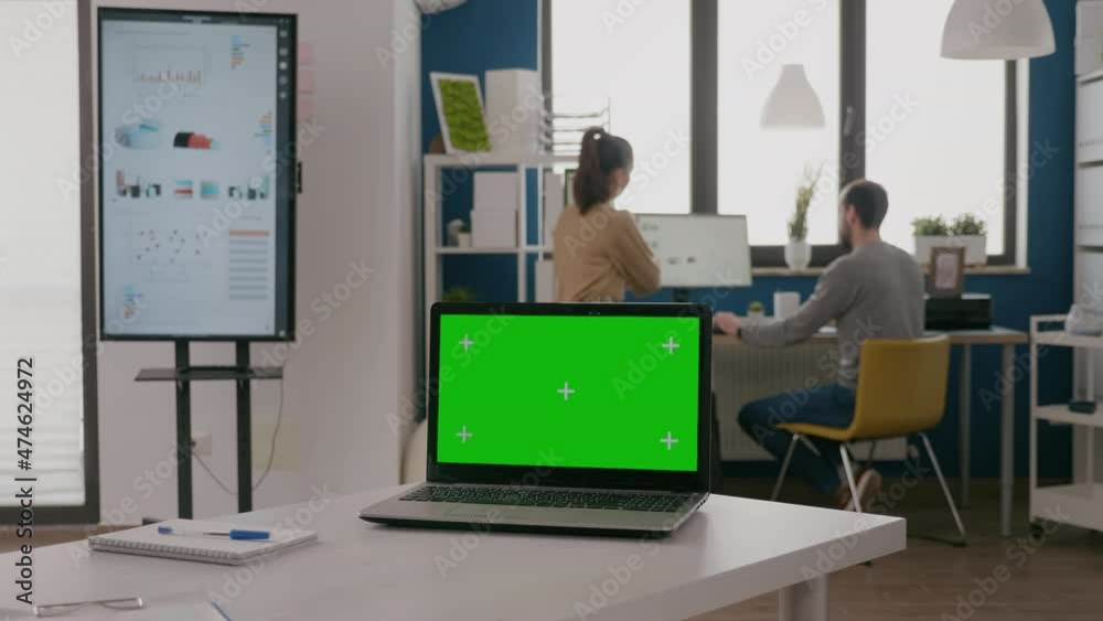 Close up of laptop with green screen at empty desk in office. Computer with chroma key on ...