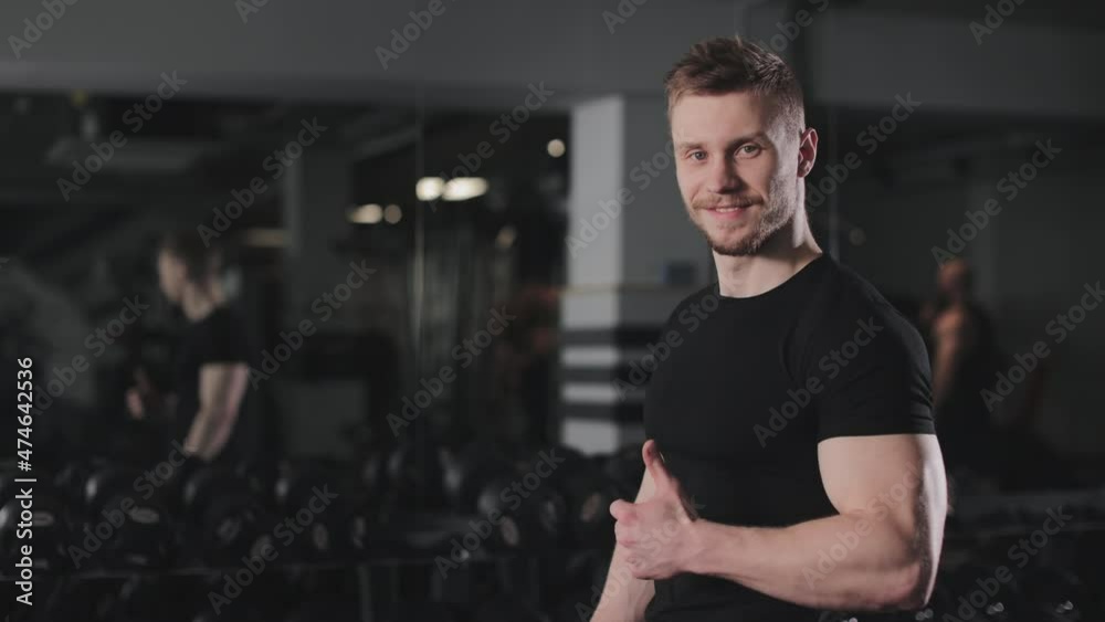 A sporty man is standing in the gym and looking at the camera. He is ...