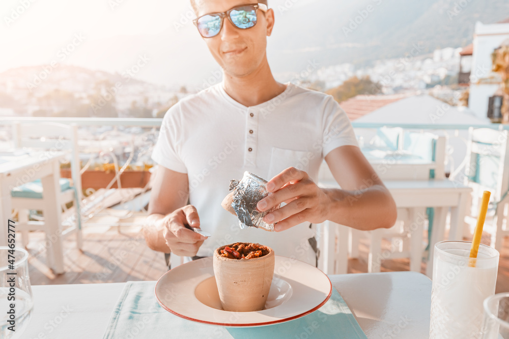 Young man eating Testi kebab in restaurant on a terrace. It is an ...