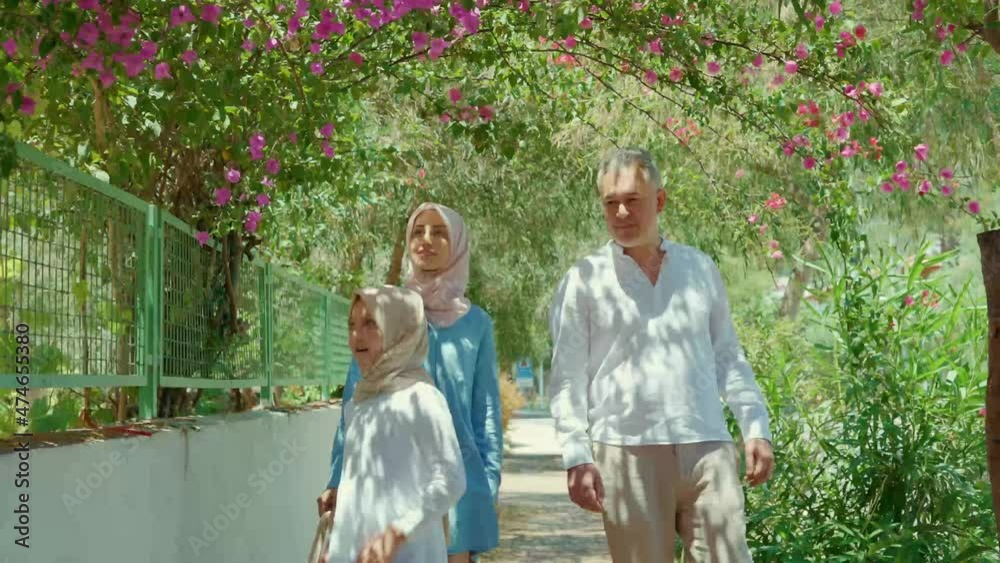 A Muslim family taking a weekend walk on a flowery road on a summer day ...