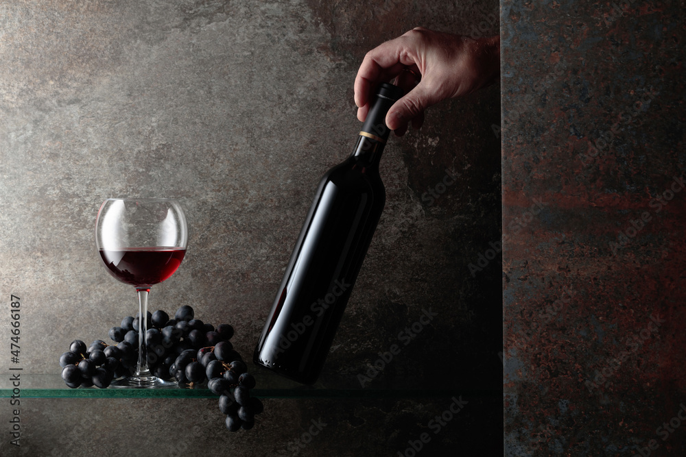 Hand reaches for a bottle of red wine. Stock Photo | Adobe Stock