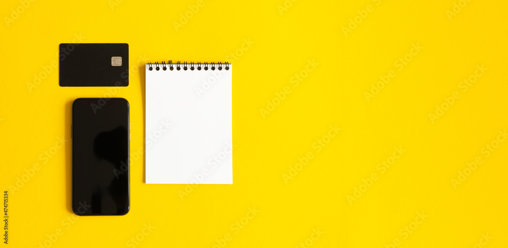 Smartphone, credit card, notepad on yellow background with copy space ...