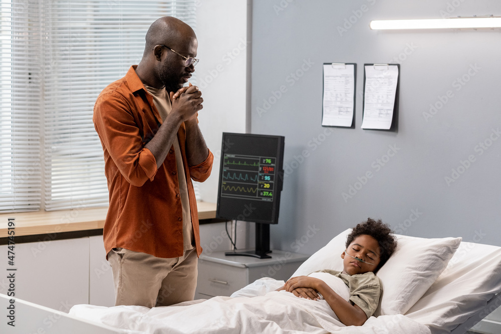 Foto de African father looking at his sick son and praying for his ...