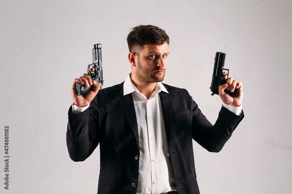 A young guy in a black suit with a gun in his hands on a white ...