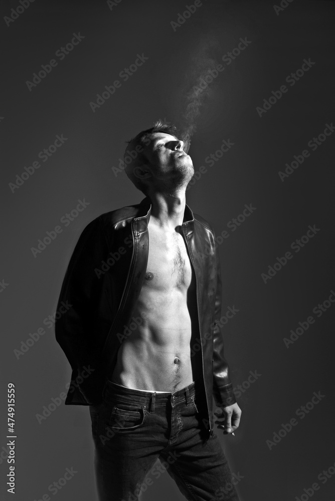 Young fashion model in leather jacket smoking a cigar and exhales smoke ...