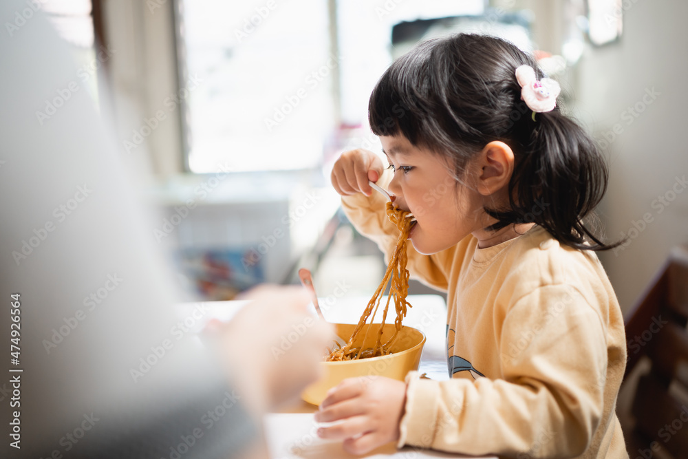 Asian baby eating delicious noodle in kitchen on dining table. Happy ...