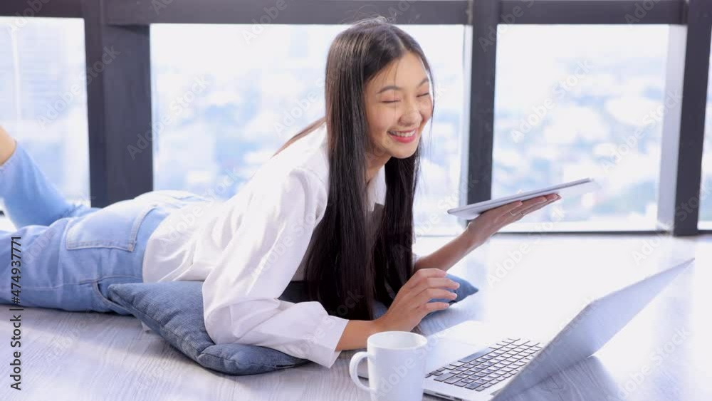 Young asian woman lying on the floor with legs up,listen watch digital class e-learning online ...