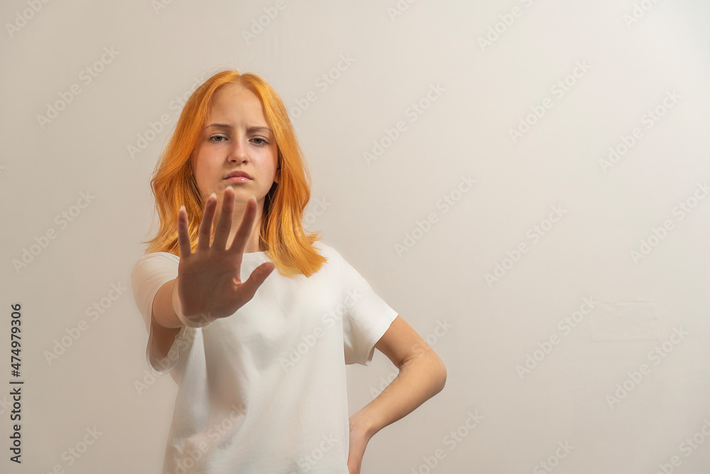 teen girl with red hair in a white t-shirt on a light background denial ...